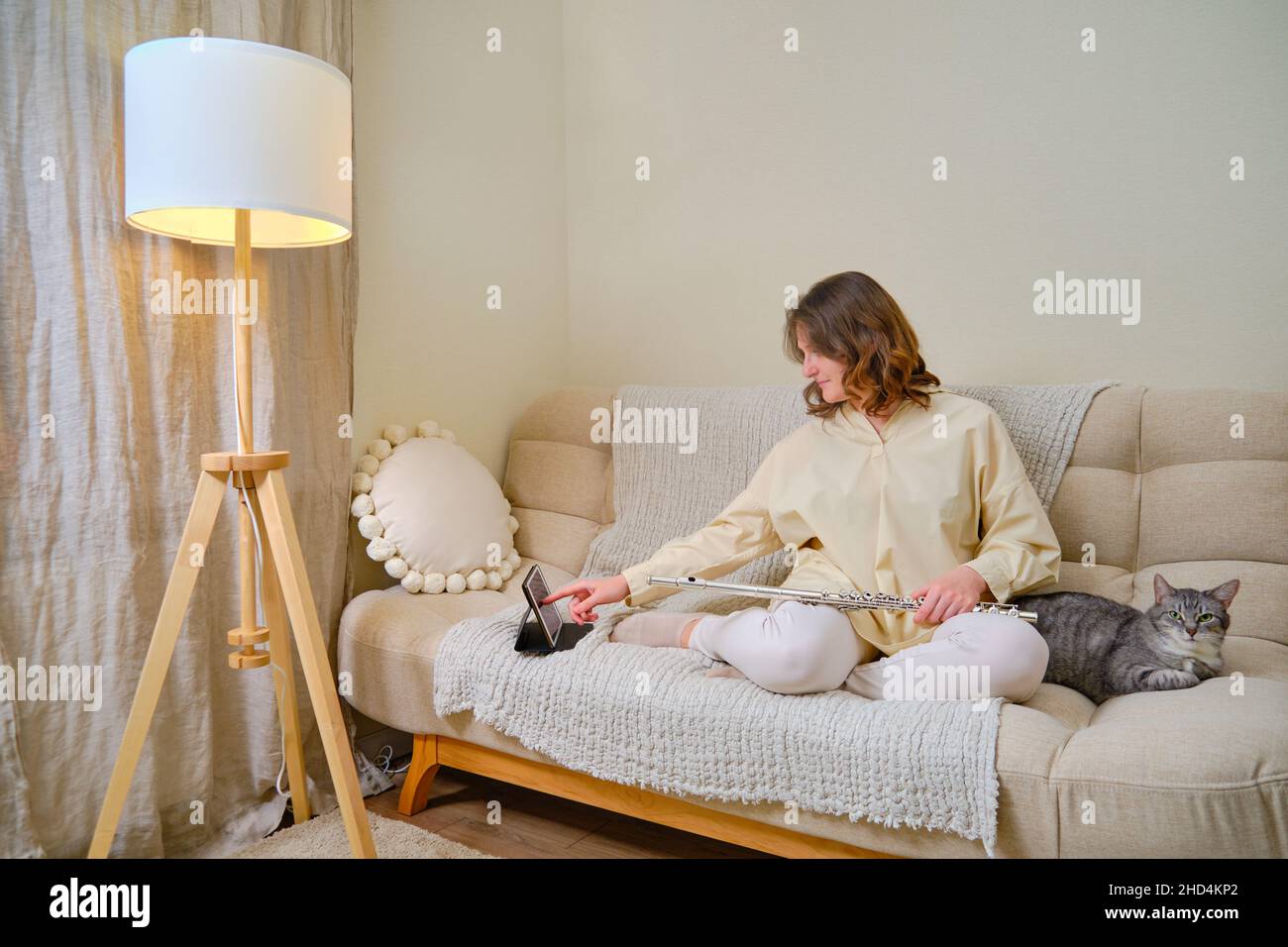 Woman musician with flute looks into tablet at home on sofa in living ...