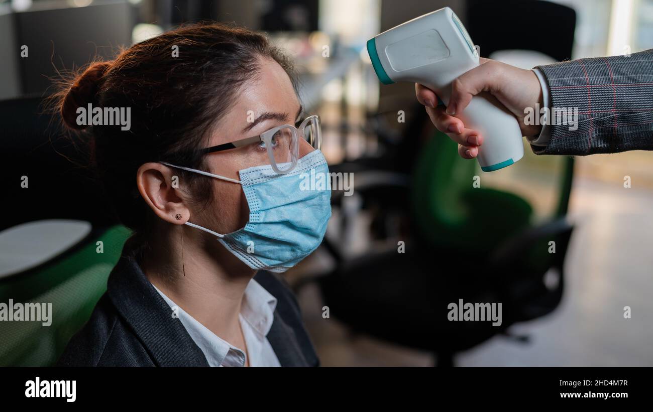 Doctor measures the temperature of an office worker with an infrared ...