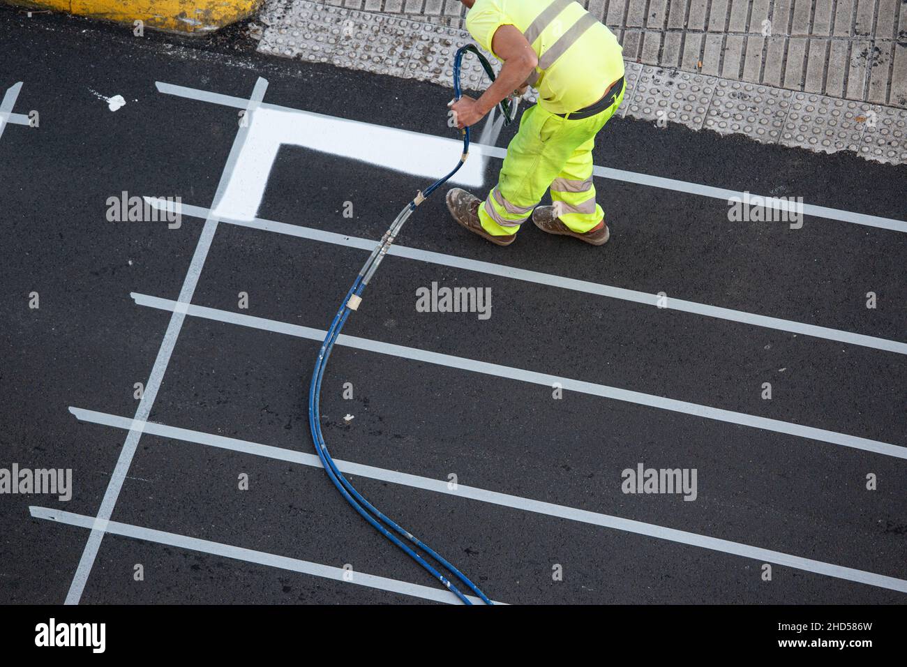 Worker painting a pedestrian crosswalk road using paint sprayer gun ...