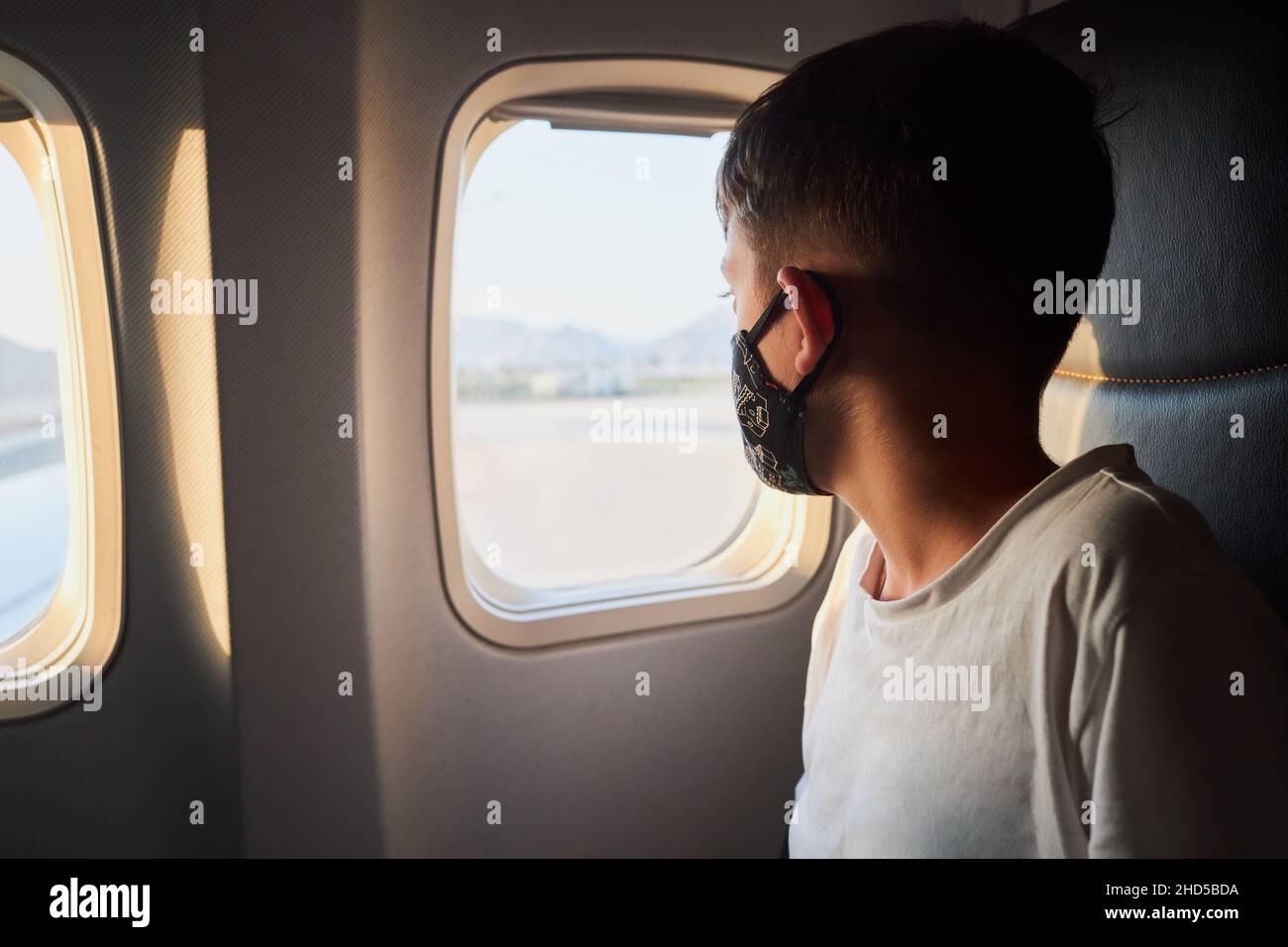 Caucasian boy is looknig into the plane porthole before the flight ...
