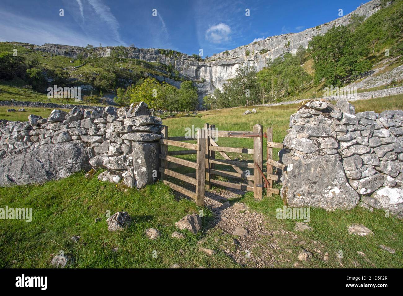 A gate and path leading through a dry stone wall to a limestone cliff ...