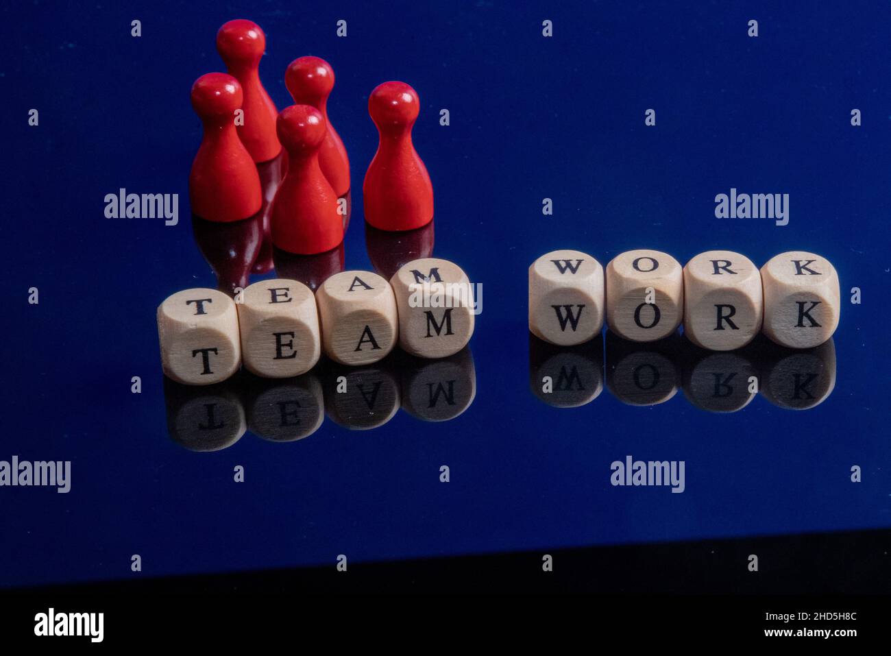 White letter cubes forming the word Teamwork in front of mirroring blue ...