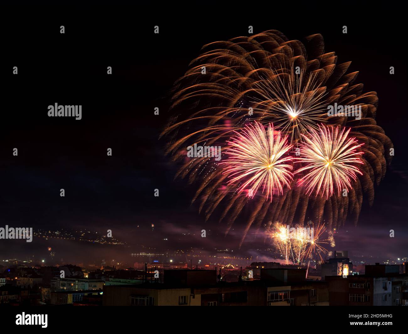 Bright New Year fireworks sparkles in the dark sky over city. The small ...