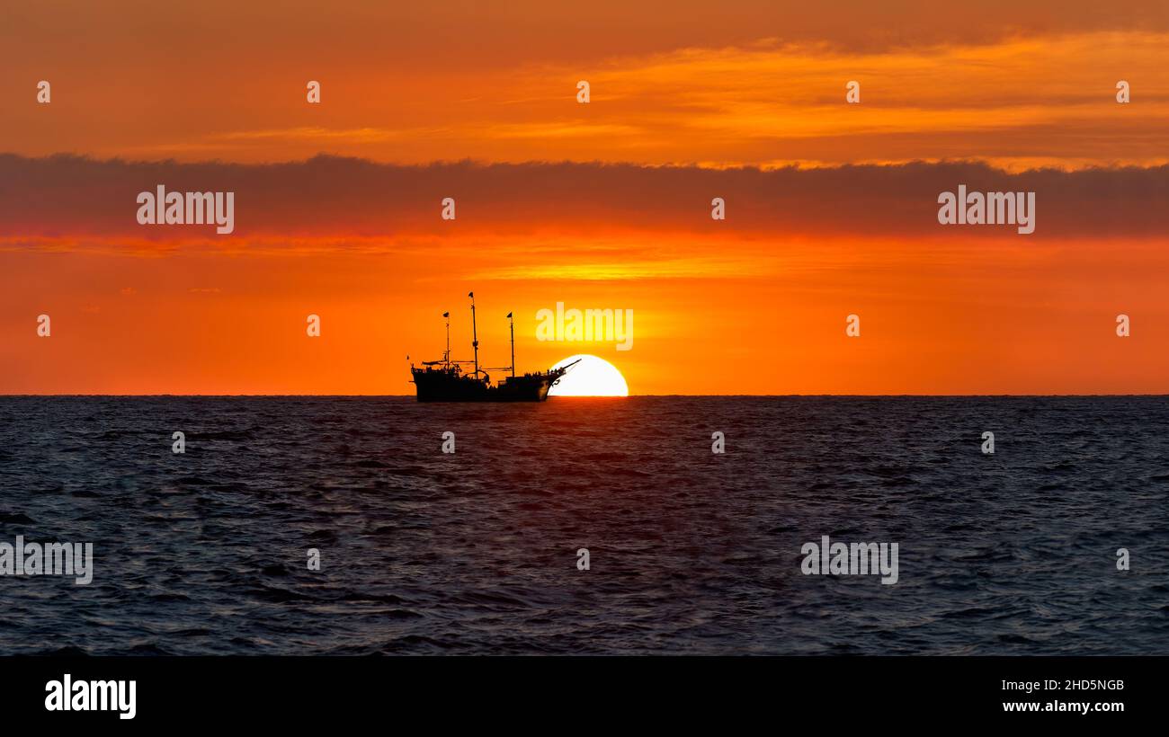 A Pirate Ship Sits On The Ocean Silhouetted Against A Colorful Orange ...