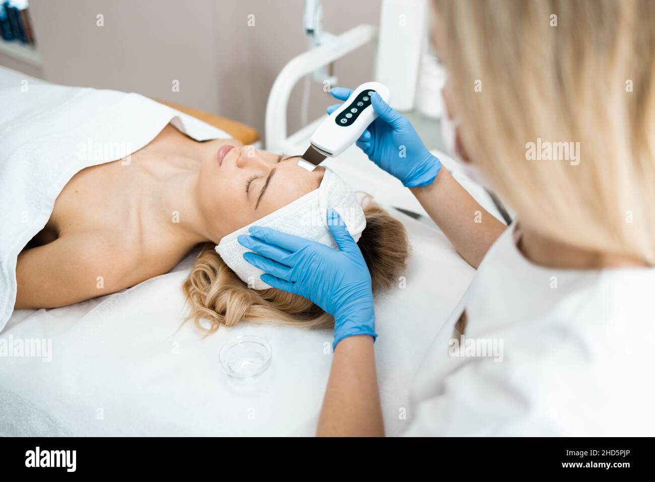 Cosmetologist in blue gloves does ultrasound cleaning of a woman's face ...