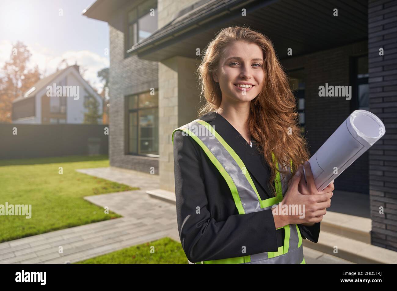 Cheerful female construction engineer with blueprints smiling to camera ...