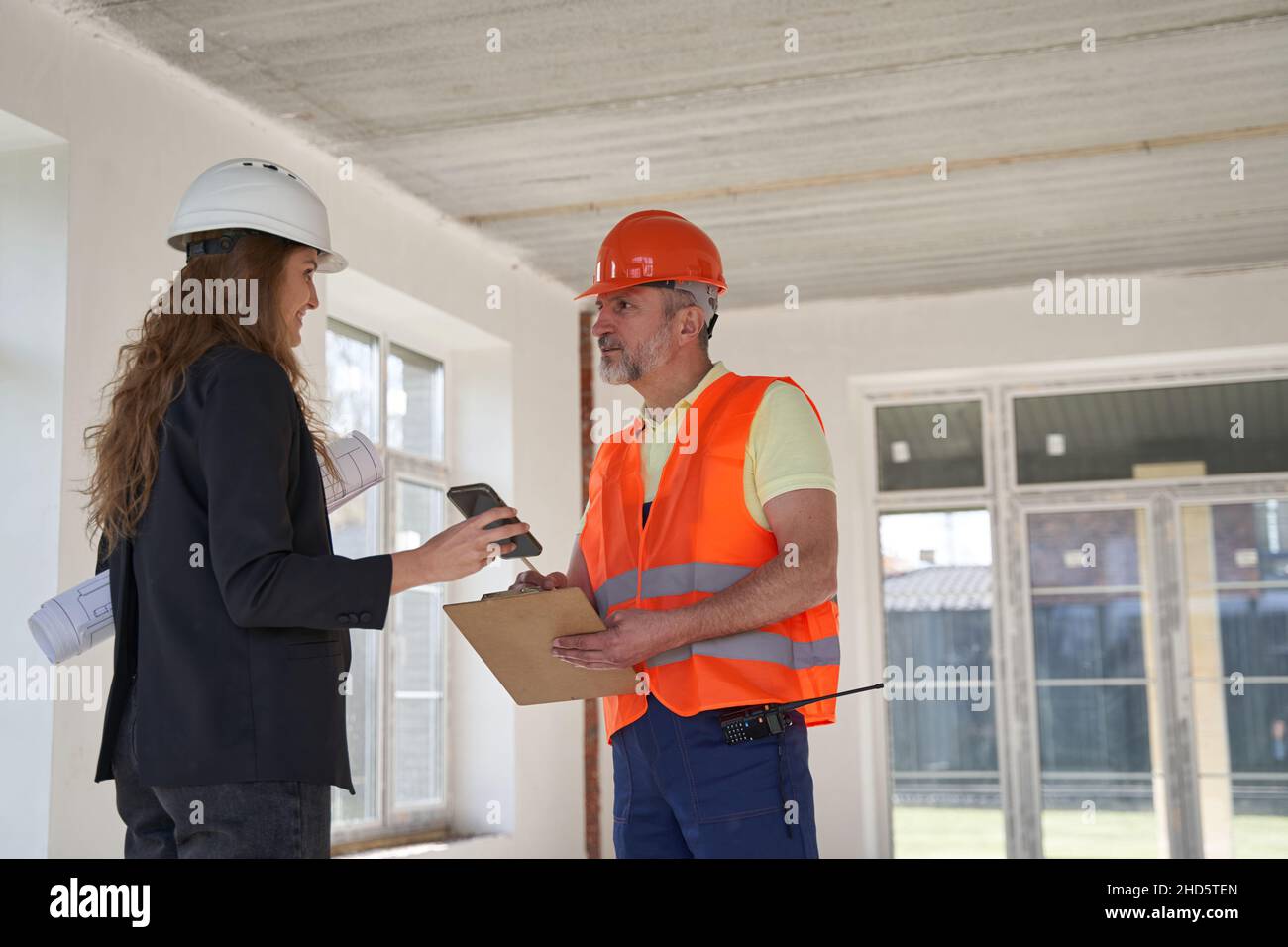 Confused construction worker looking at engineer while writing from ...