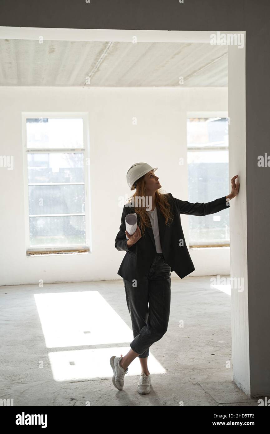 Woman looking at wall while standing with blueprints in room Stock ...