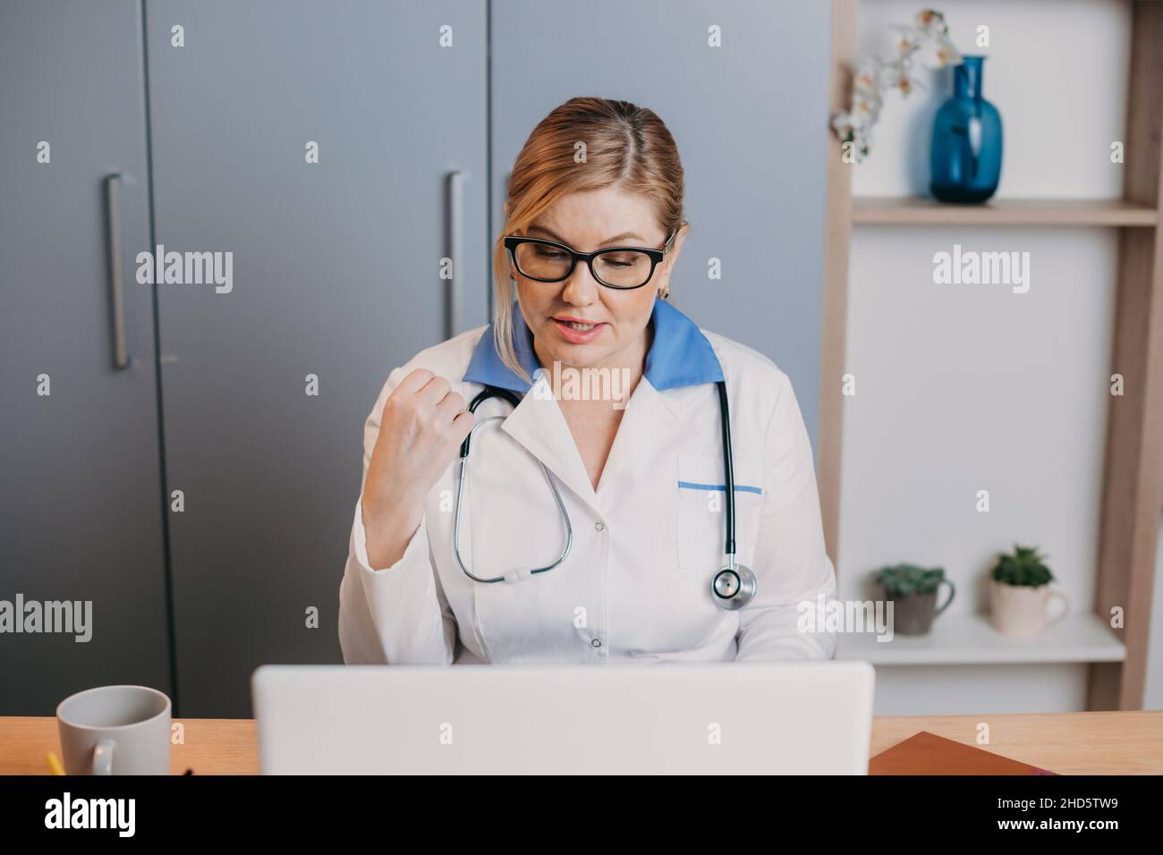Nurse wears white coat and headset speaking videoconferencing on laptop ...
