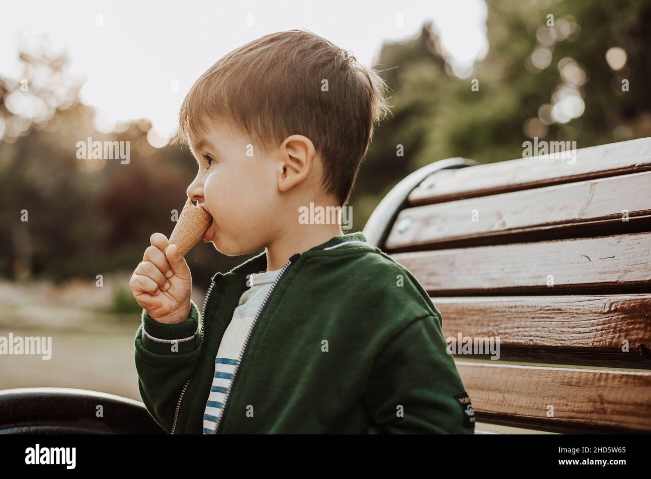 Portrait of a small baby eating icecream in park sitting on bench. Side ...
