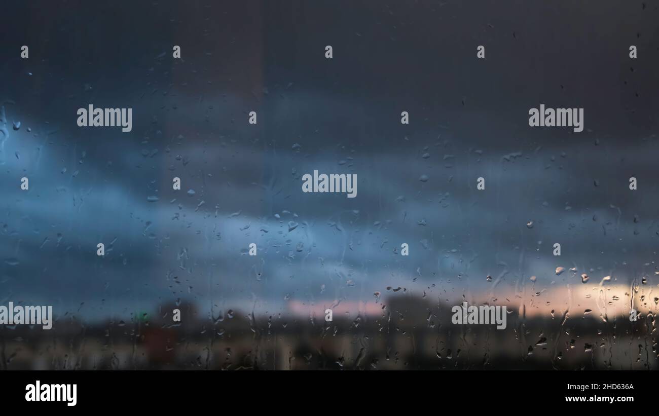Rainy day through the window on cloudy grey sky and city buildings ...