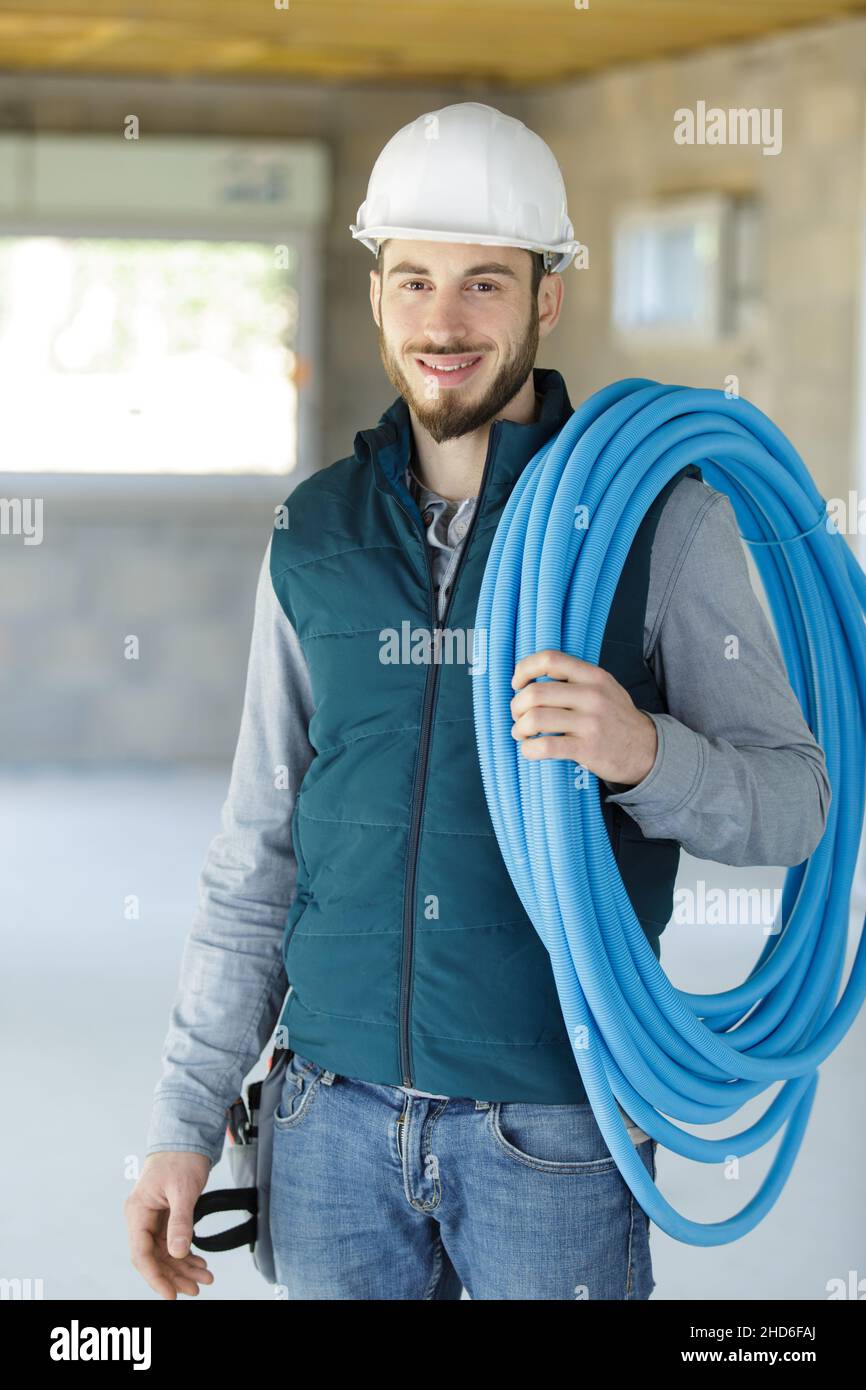 male tradesman with reel of blue pipe on his shoulder Stock Photo - Alamy