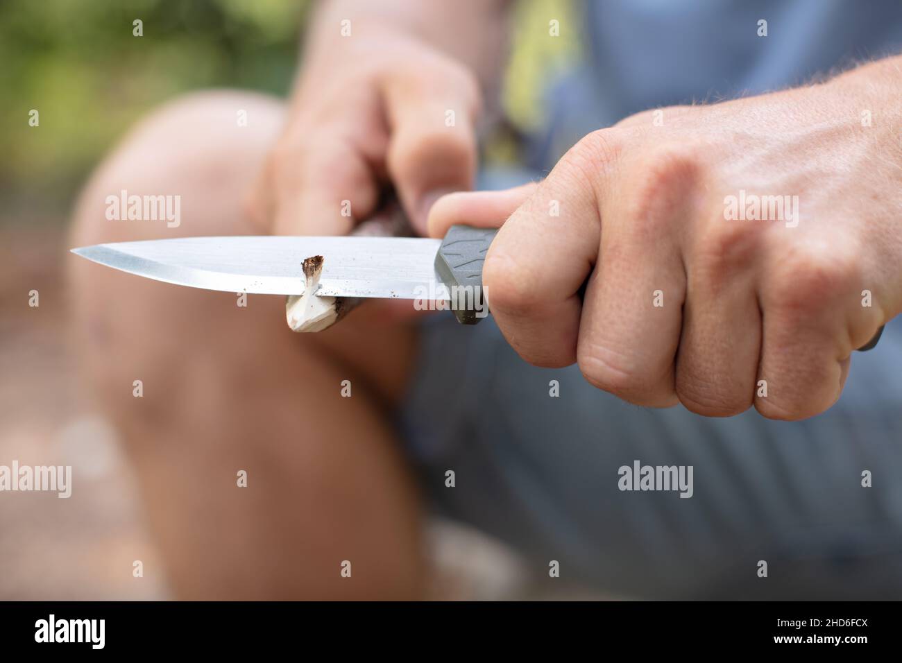 man is sharpening a stick with a knife Stock Photo - Alamy