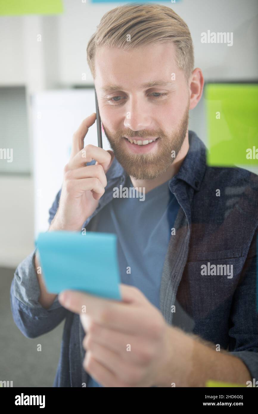 man making telephone call and reading post-it note reminder Stock Photo ...