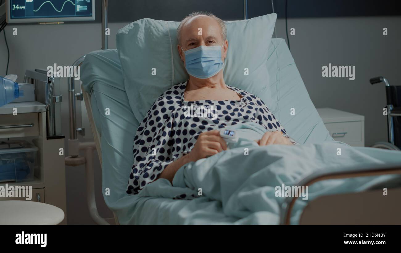 Old patient with face mask and oximeter laying in hospital ward bed at ...
