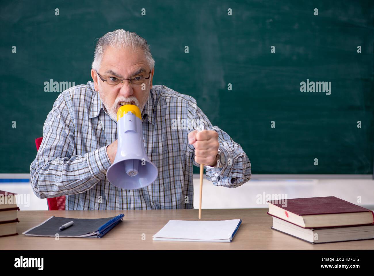 Aged male teacher holding megaphone in the classroom Stock Photo - Alamy