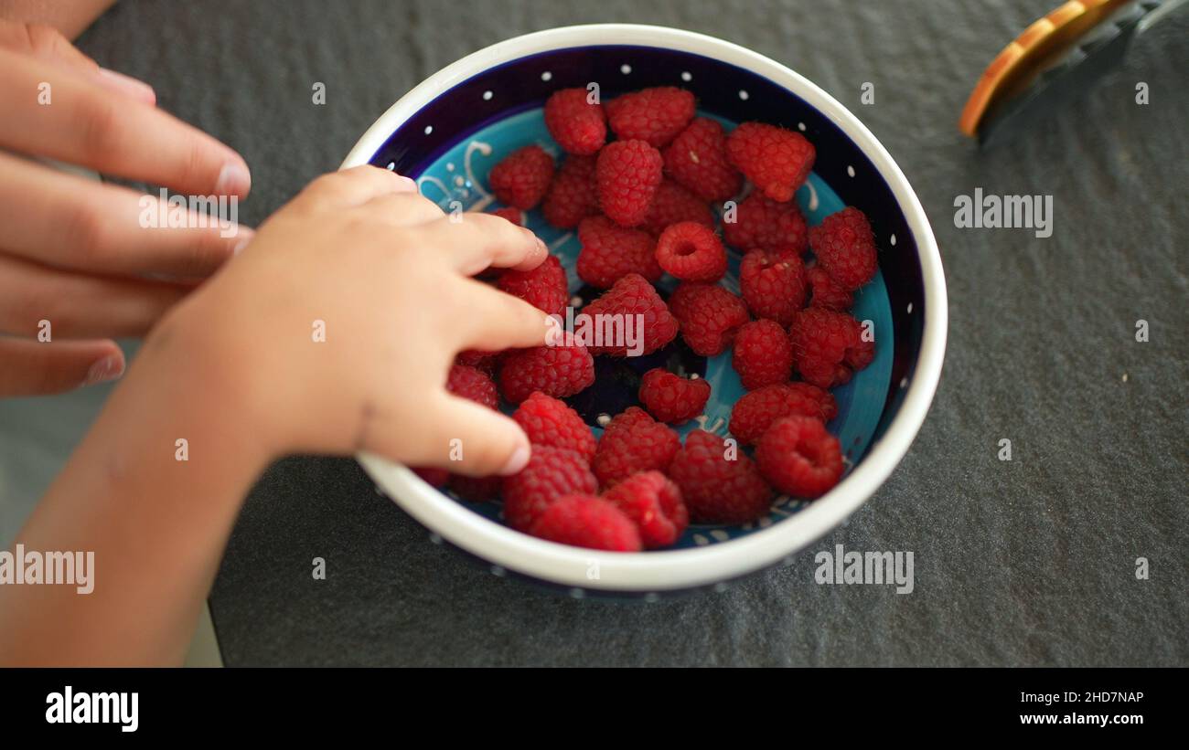 Child hands grabbing raspberries from bowl Stock Photo - Alamy
