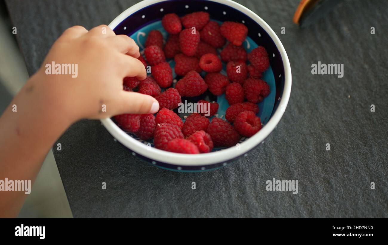 Hand grabbing raspberry fruit from bowl Stock Photo - Alamy