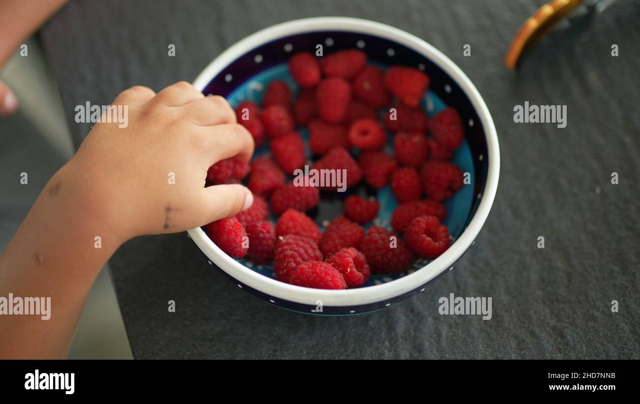 Hand grabbing raspberry fruit from bowl Stock Photo - Alamy