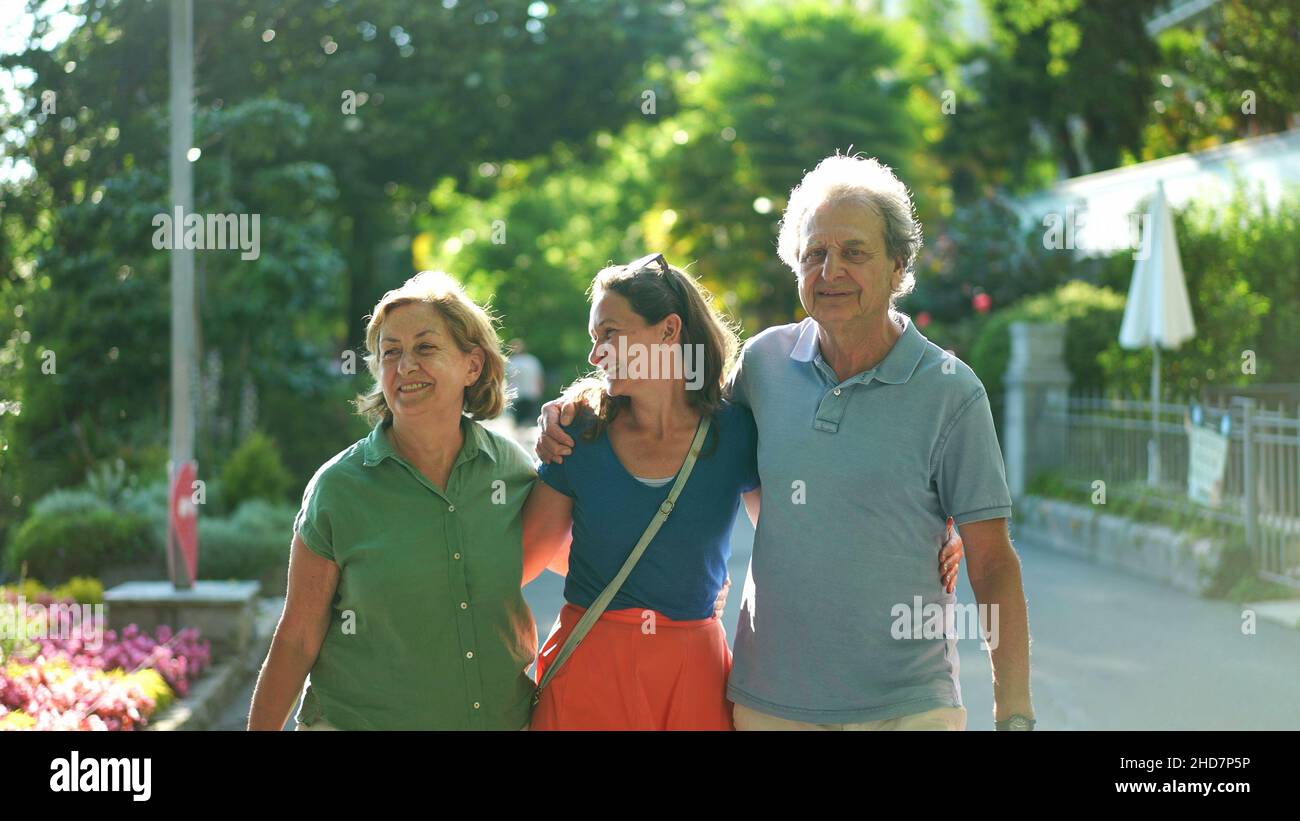 Joyful daughter walking with senior parents together in green city laughing and smiling Stock ...