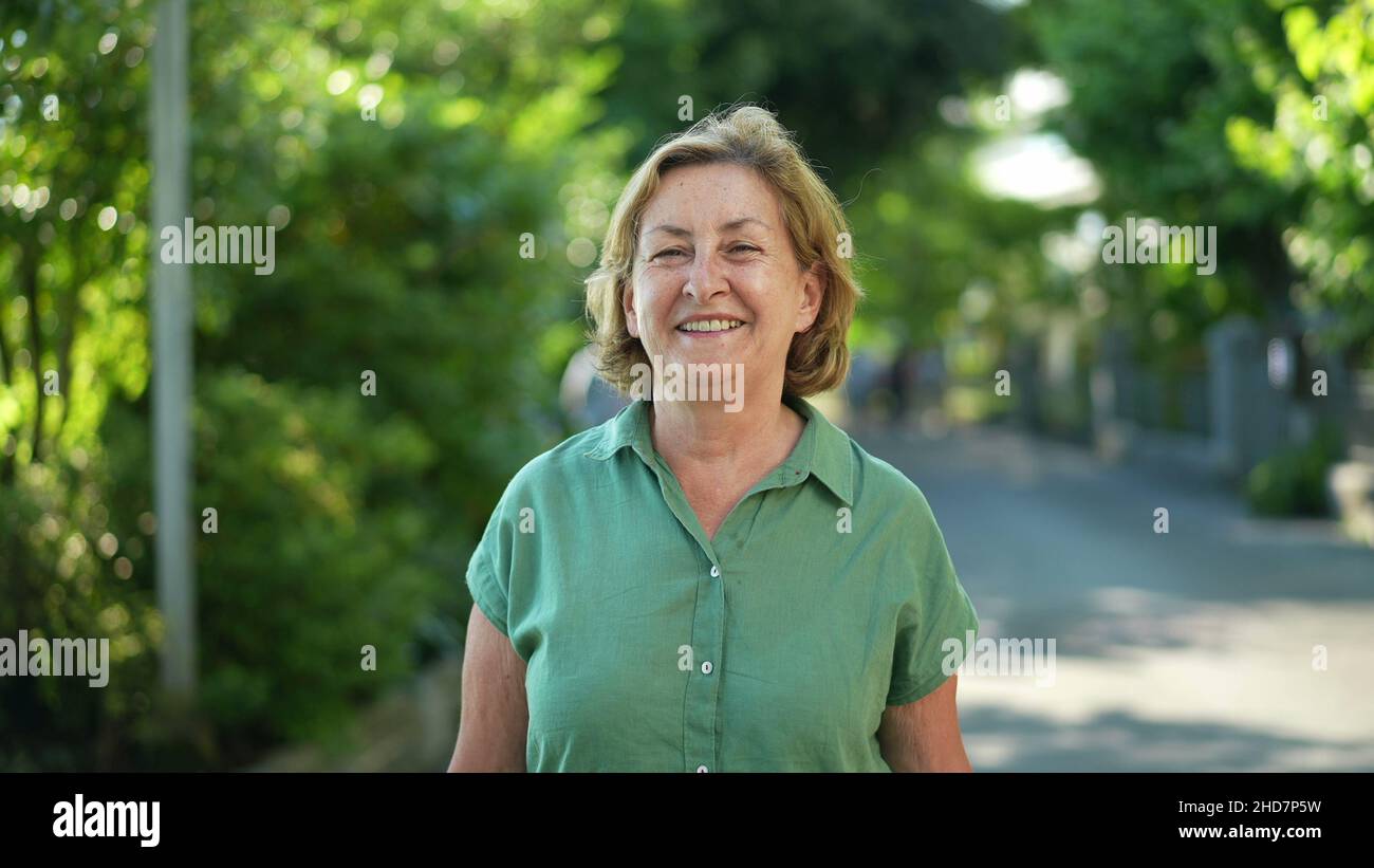 Happy senior woman walking forward smiling in city nature Stock Photo ...