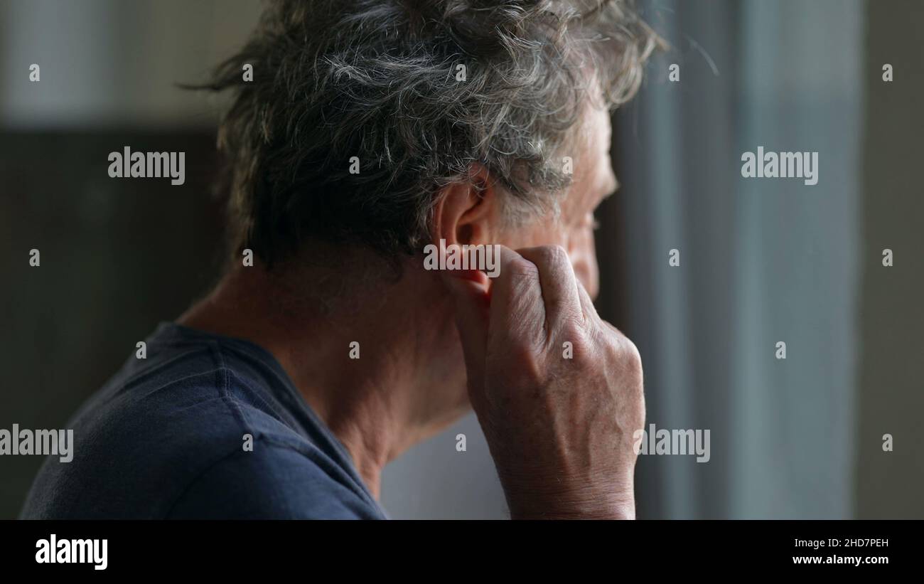 Older man touching ear scratching earlobe standing by window Stock ...