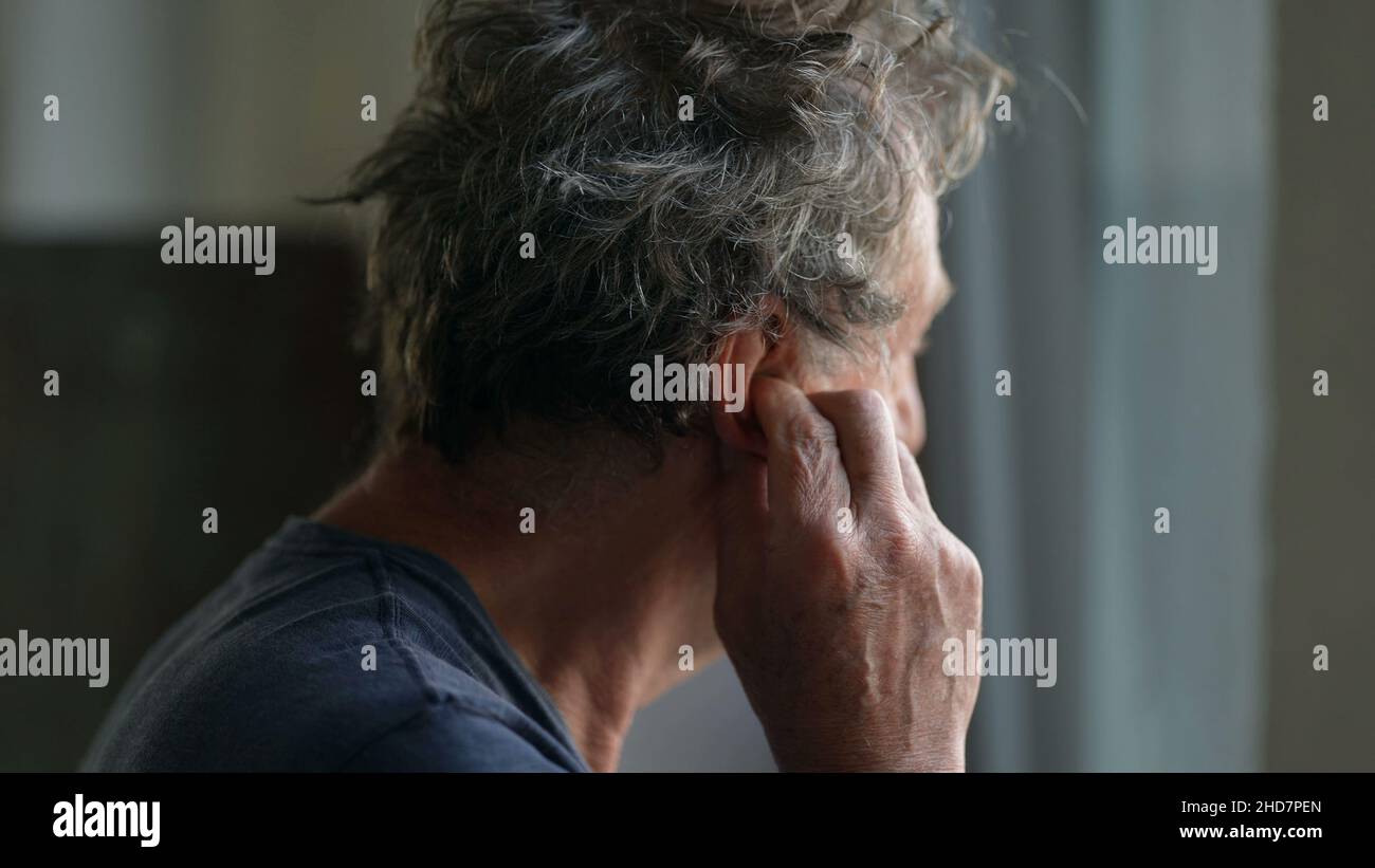 Older man touching ear scratching earlobe standing by window Stock ...
