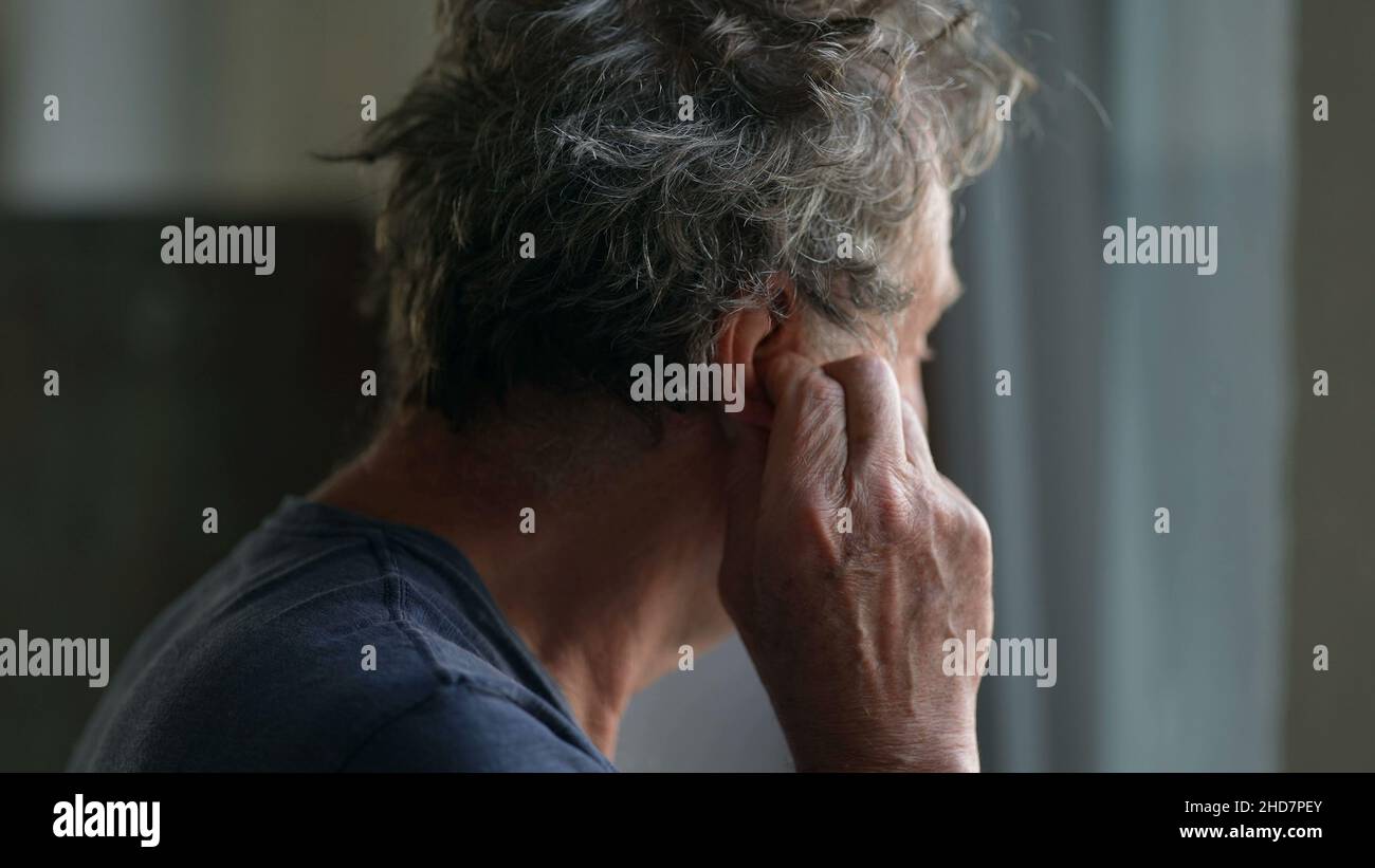 Older man touching ear scratching earlobe standing by window Stock ...
