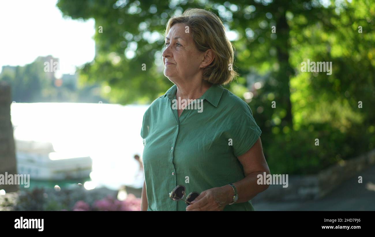 Older woman walking outdoors in green urban city, senior person walks ...