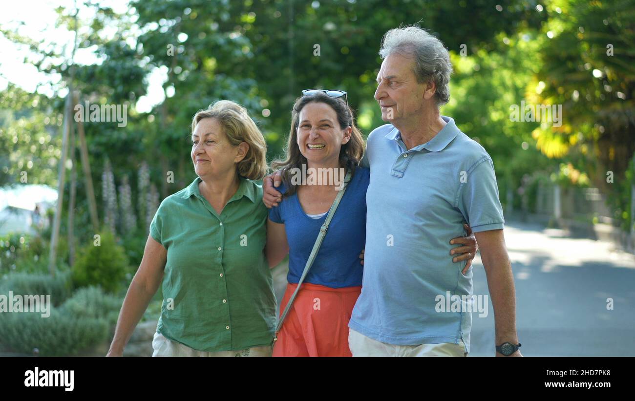 Parents walking with adult daughter together, family day walk outside ...