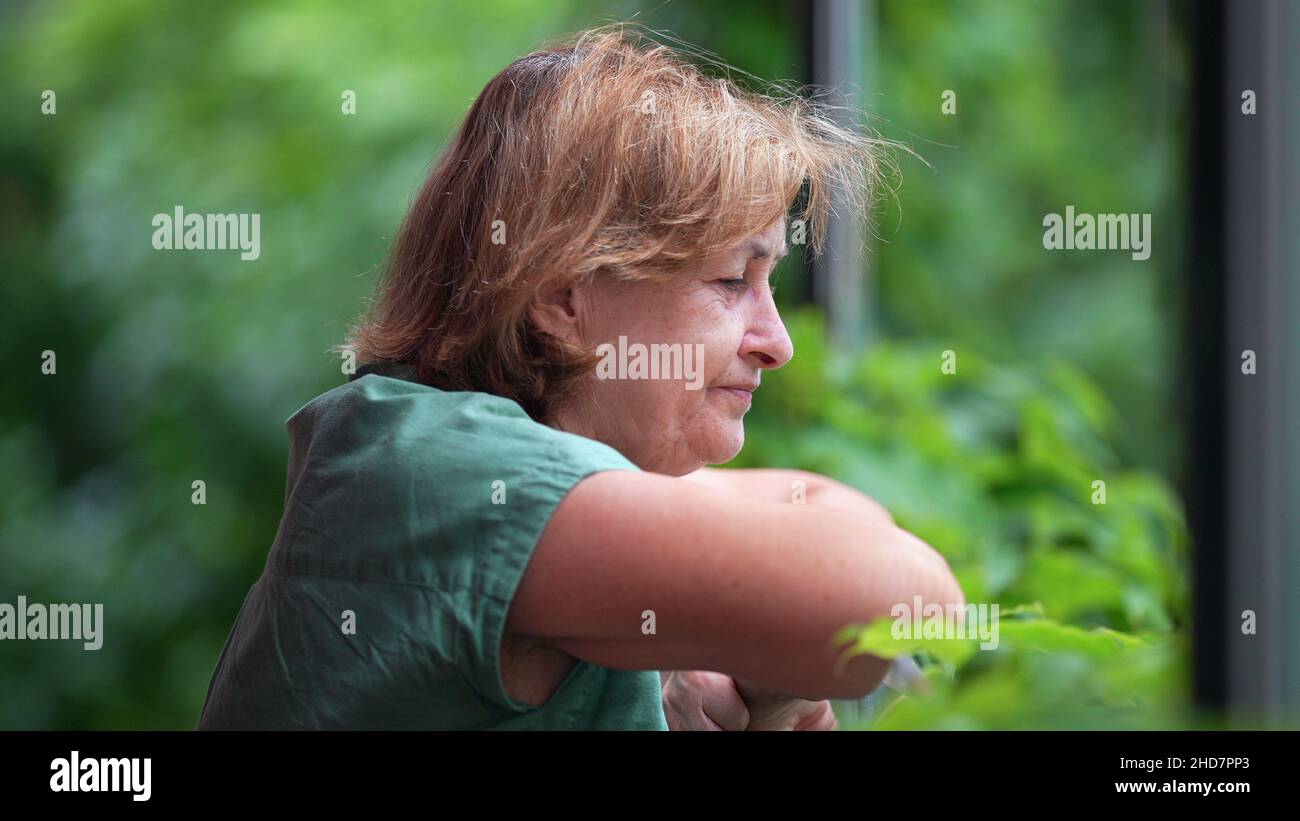 Pensive senior woman standing outside looking out from balcony Stock ...