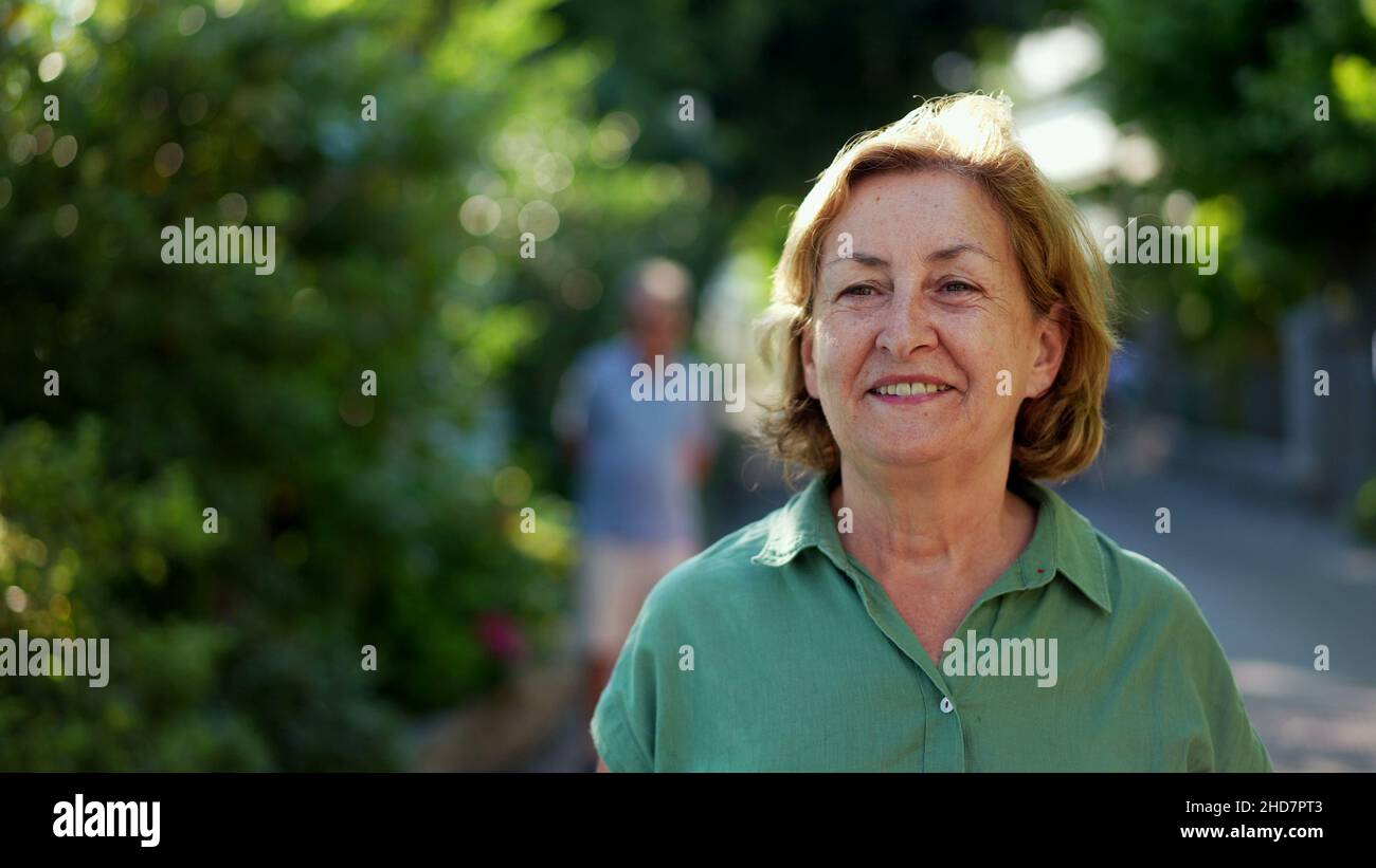 Portrait senior woman walking outside in green city Stock Photo - Alamy