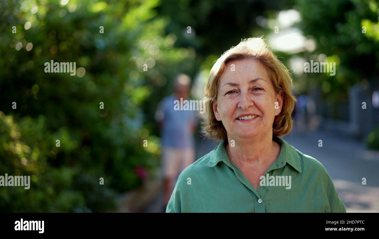 Portrait senior woman walking outside in green city Stock Photo - Alamy