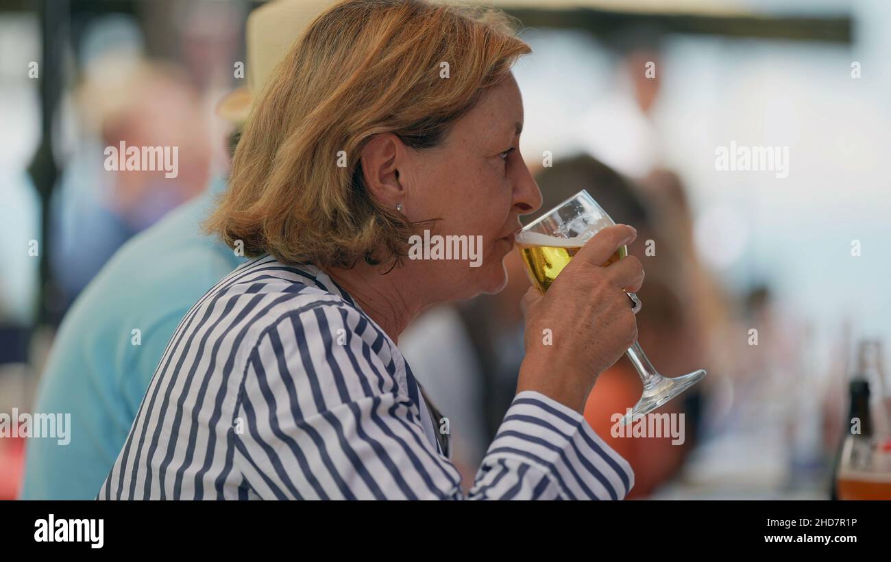 Senior woman drinking glass beer seated at restaurant. Older lady takes ...