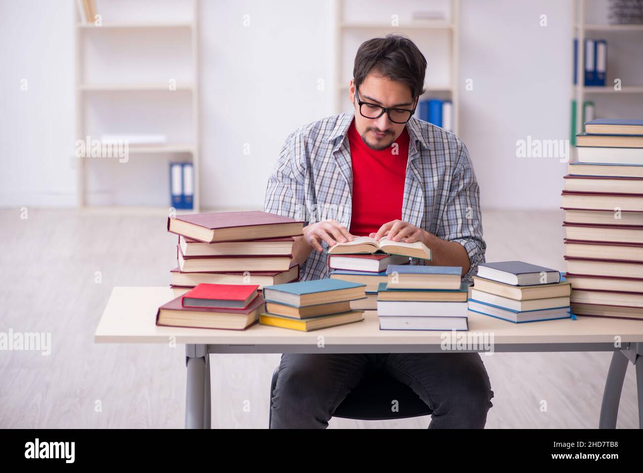 Young student and too many books in the classroom Stock Photo - Alamy
