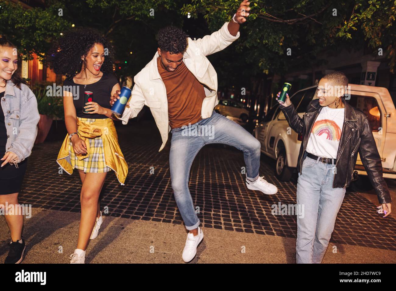 Vibrant young man showing his friends some dance moves at night. Group ...