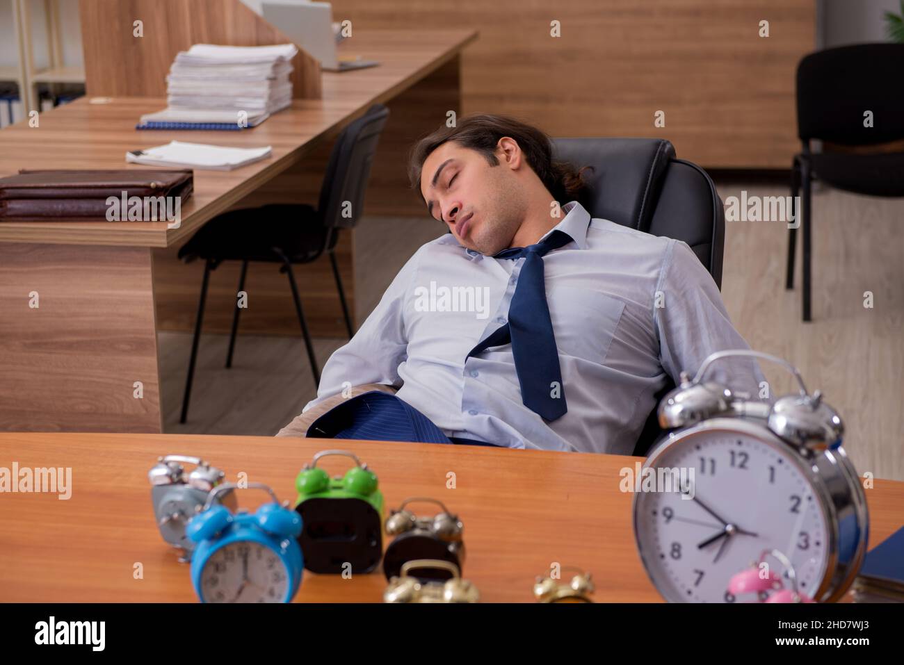 Young businessman sleeping in the office in time management concept ...