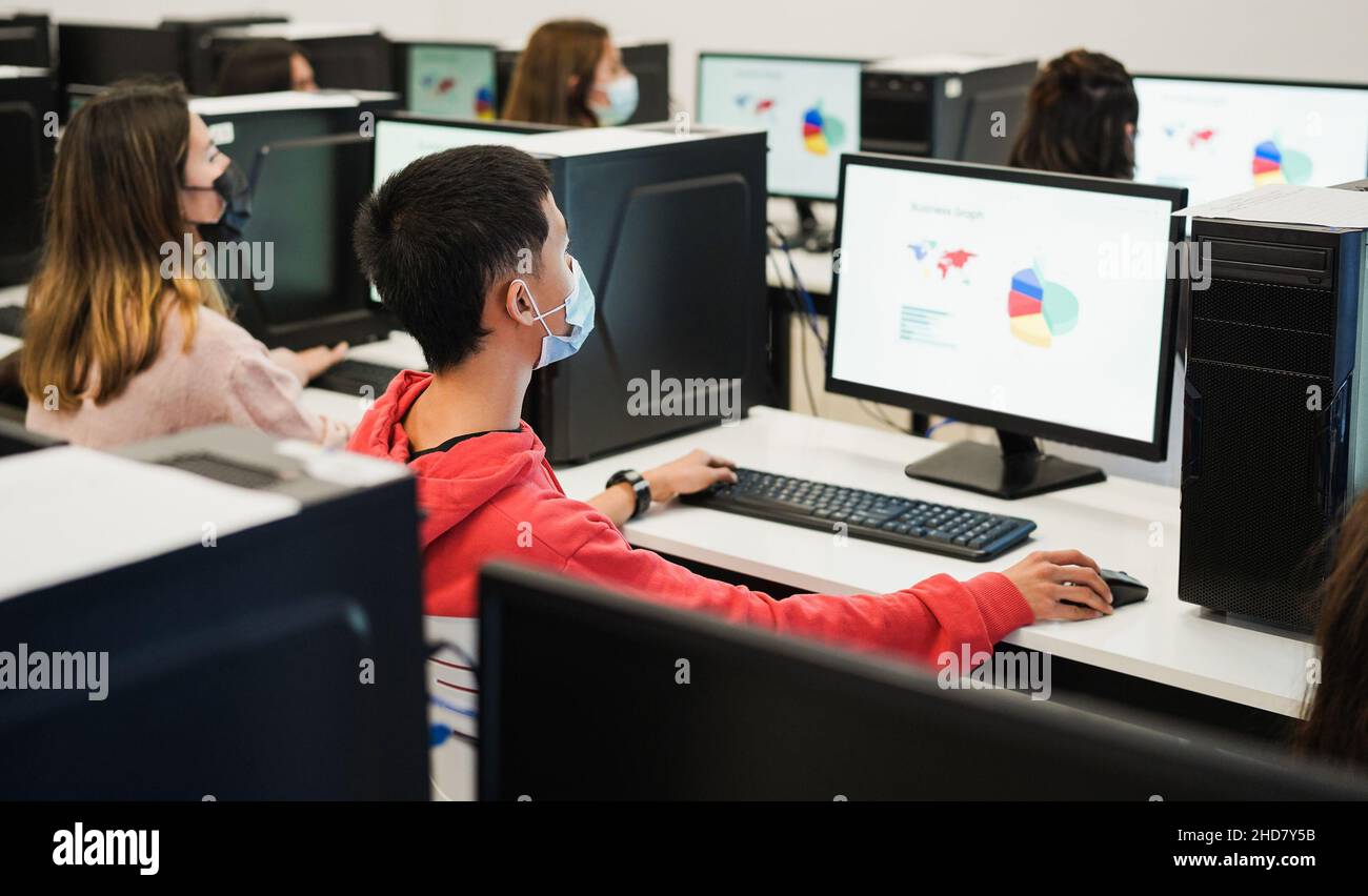 Young students using computers inside business class wearing safety ...