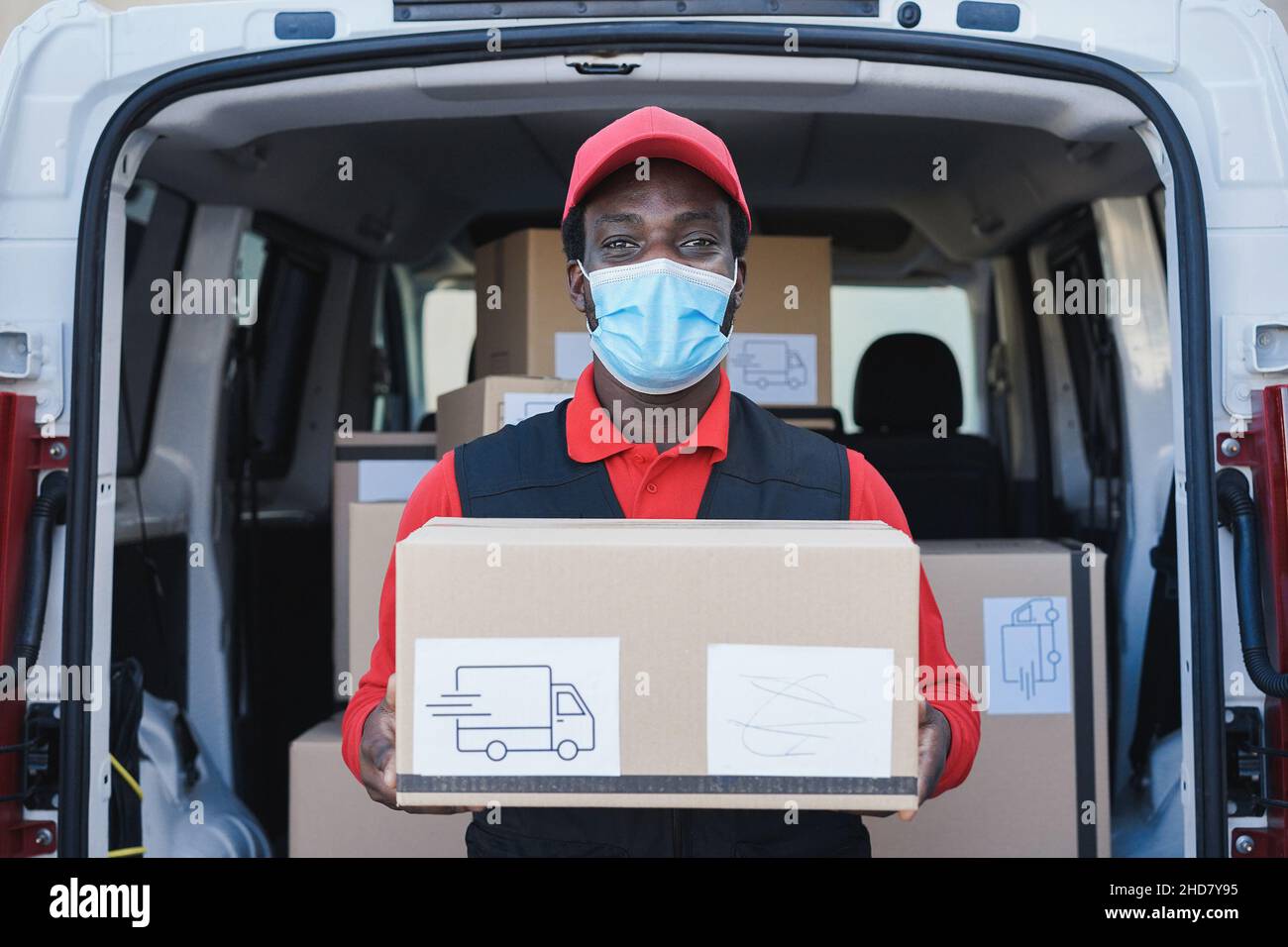 African delivery man smiling on camera while wearing safety mask ...
