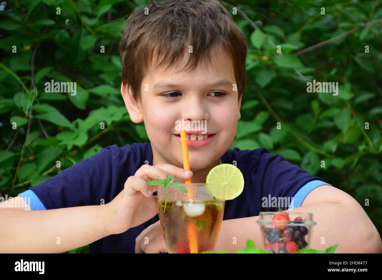 Child boy drinks natural lemonade summer drink, tea with wild berries ...