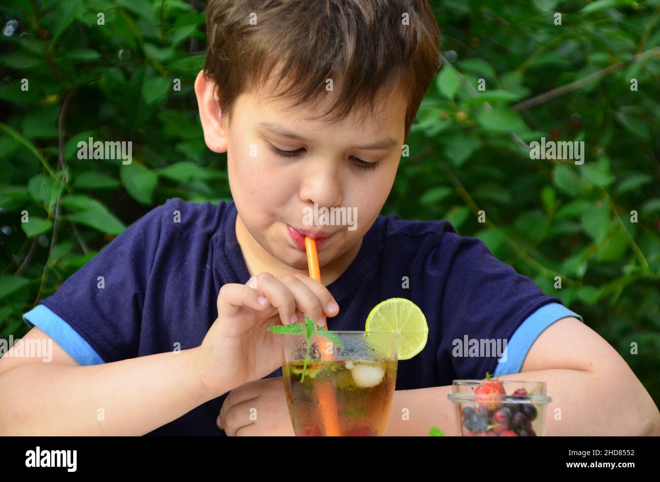 Child boy drinks natural lemonade summer drink, tea with wild berries ...