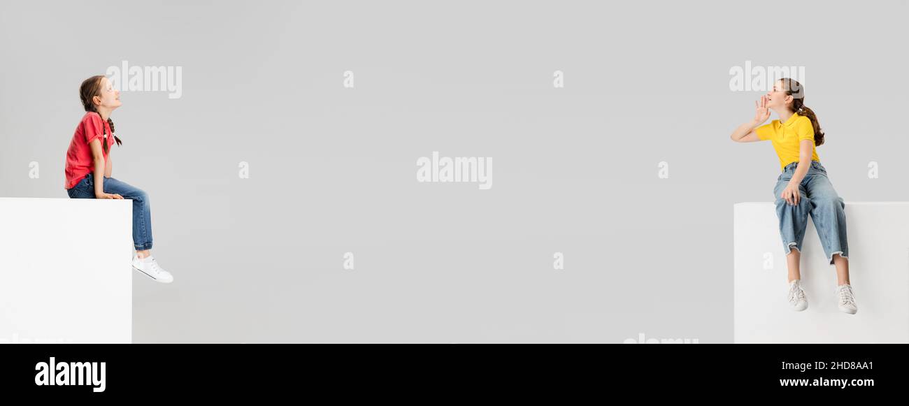 Two little girls sit opposite each other and communicate isolated on ...