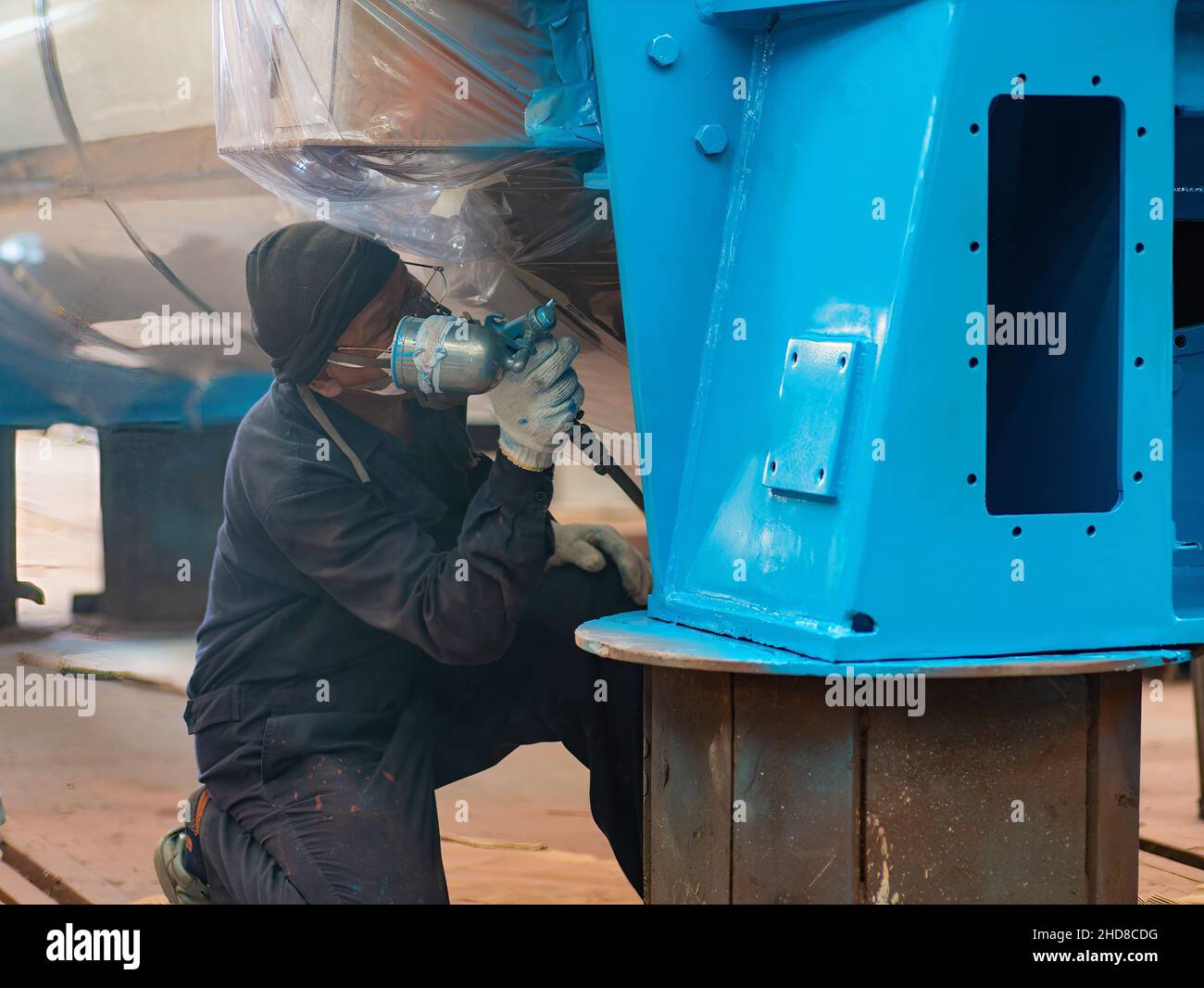 Worker spray painting heavy machinery at an industrial workshop Stock ...