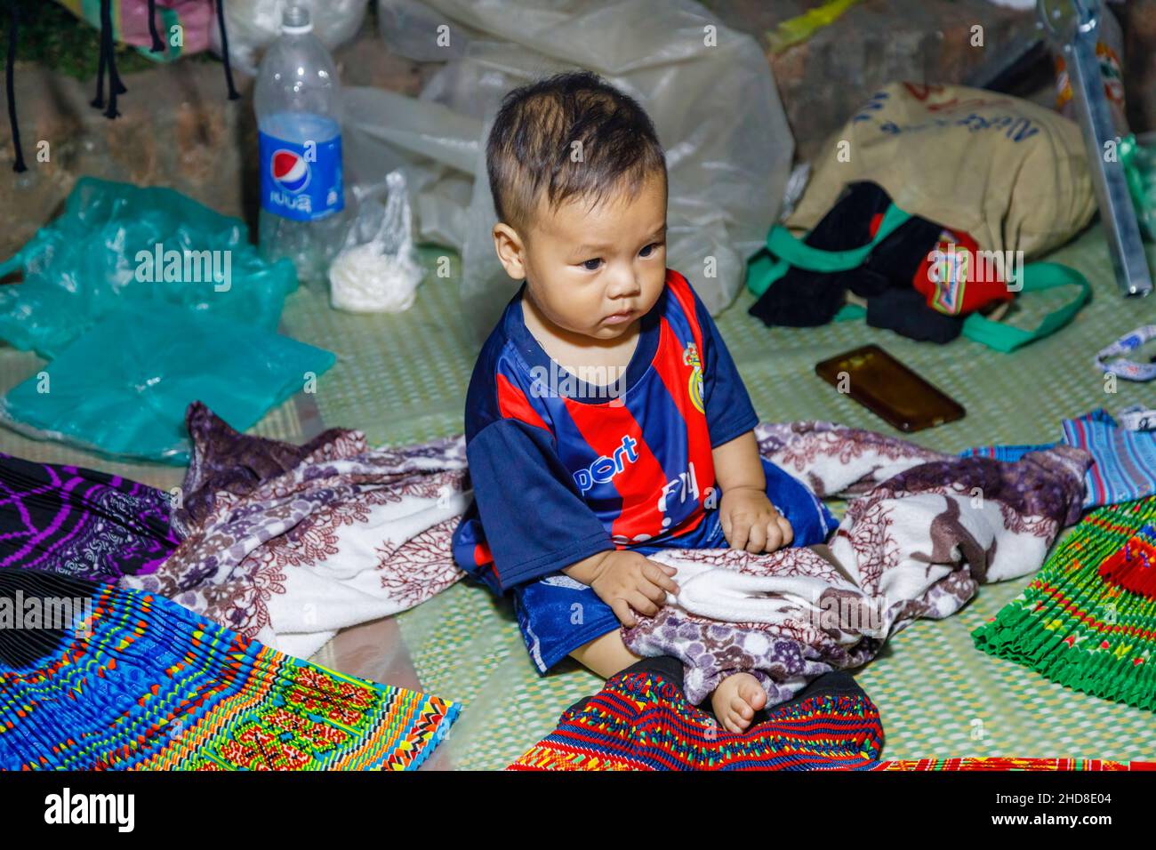 Cute local chubby baby boy sits in a stall selling fabrics in the ...