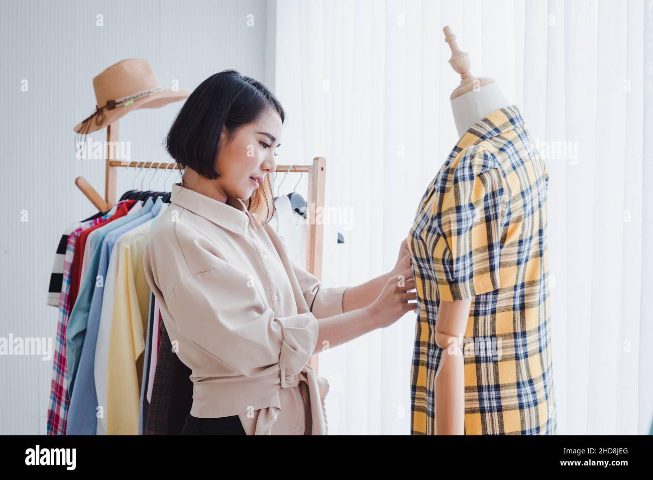 Beautiful Asian woman designer is wearing clothes for a wooden model ...