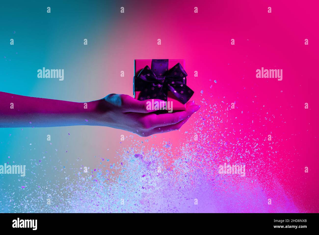 Female hand and explosion of colored, neoned powder on pink blue studio ...
