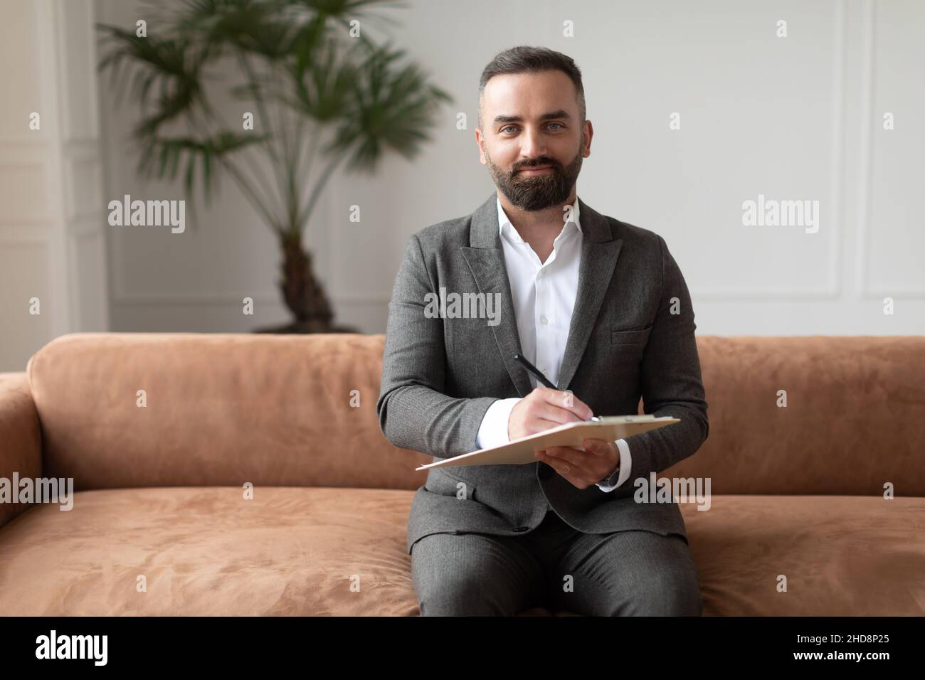 Portrait of confident male therapist in suit sitting on couch Stock ...