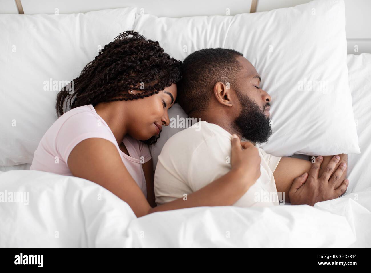 Millennial Black Female And Male Lie On Bed Sleep Hugging On Soft