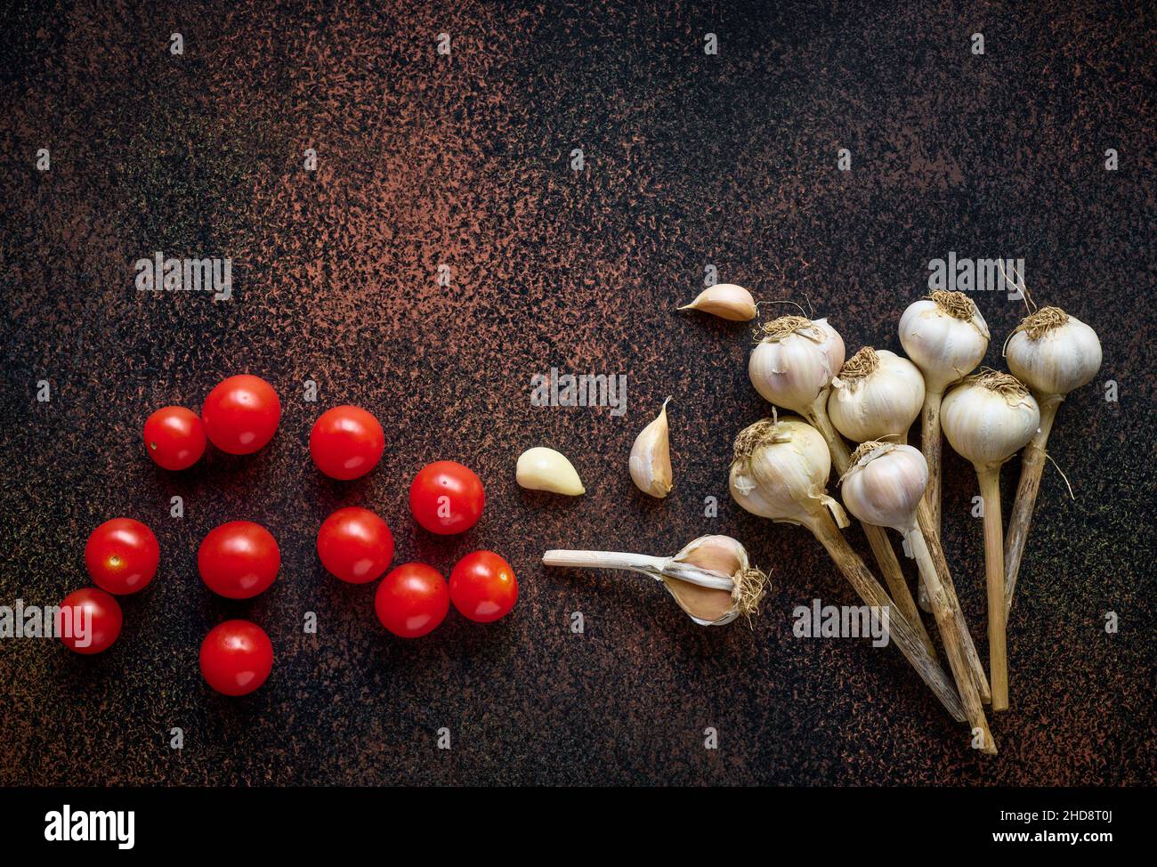 Flat lay of fresh cherry tomatoes with garlic on dark rusty background ...