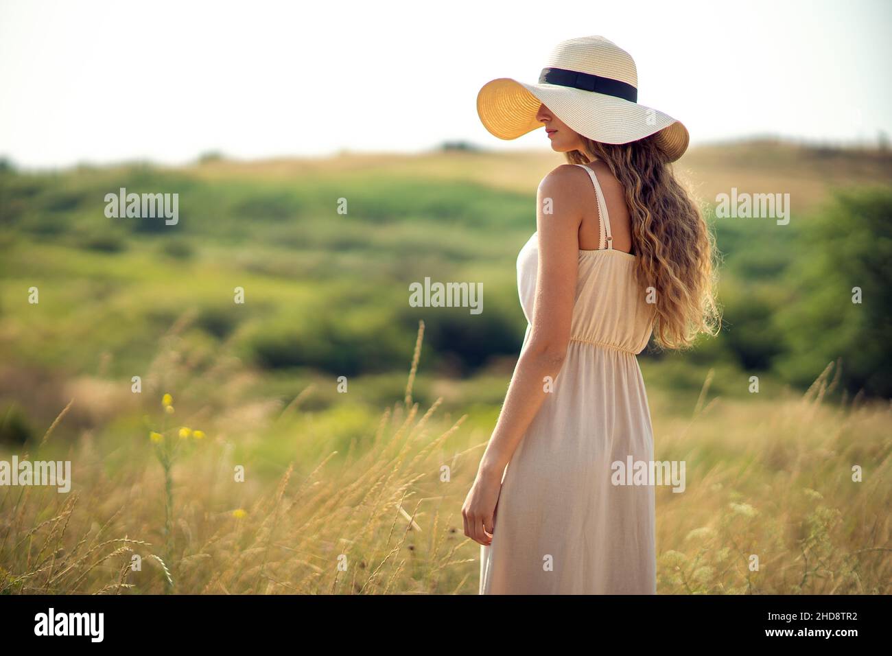 Back view of beautiful woman who walks on field while wearing a sunhat ...